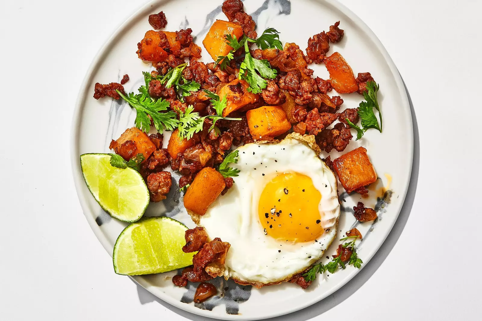 Cubed squash at crumbled chorizo hash sa marble plate na nilagyan ng sunnyside egg cilantro at lime wedges.