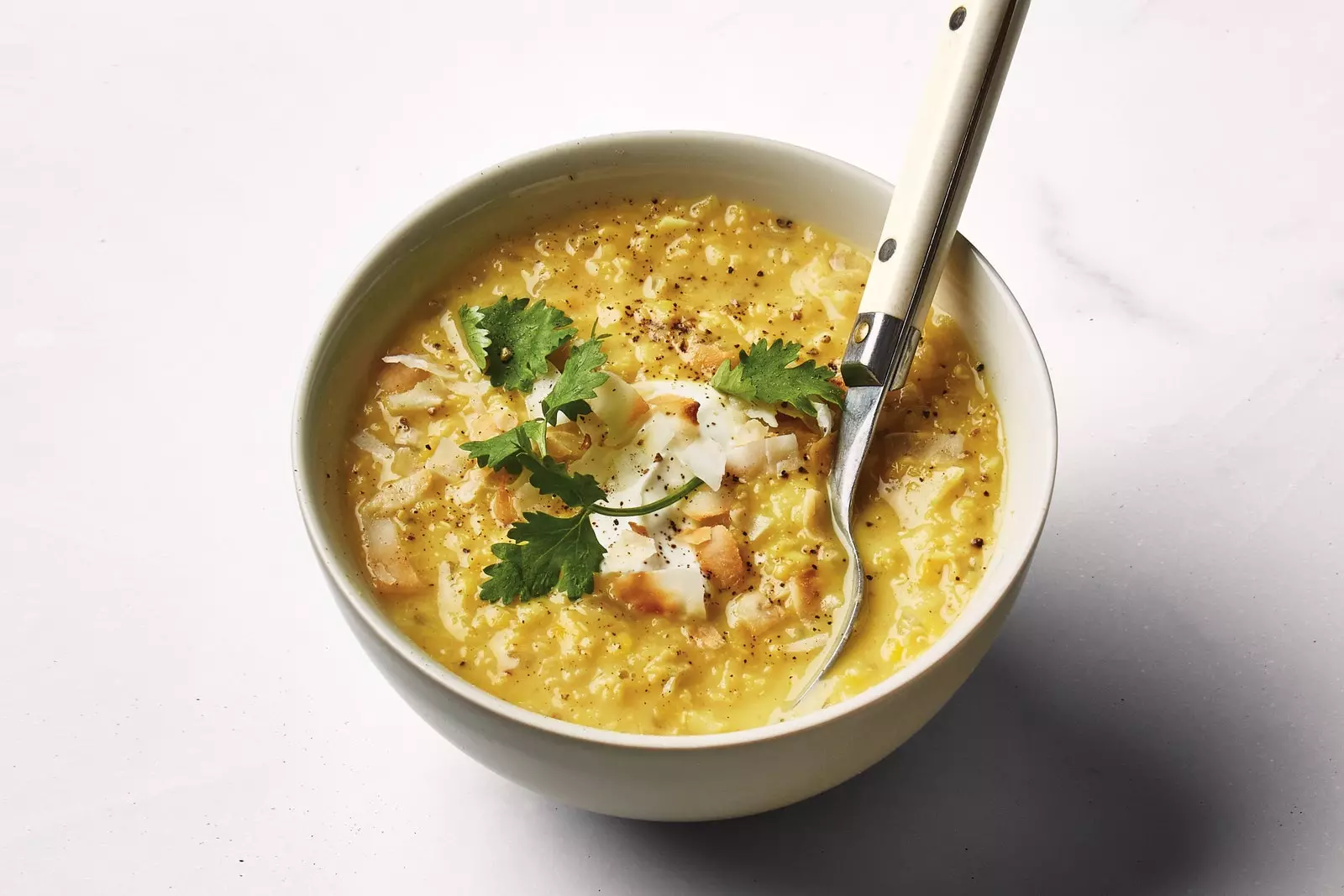 Larawan ng coconut at apple flavored lentil dal sa isang ceramic bowl na nilagyan ng toasted flaked coconut at cilantro.