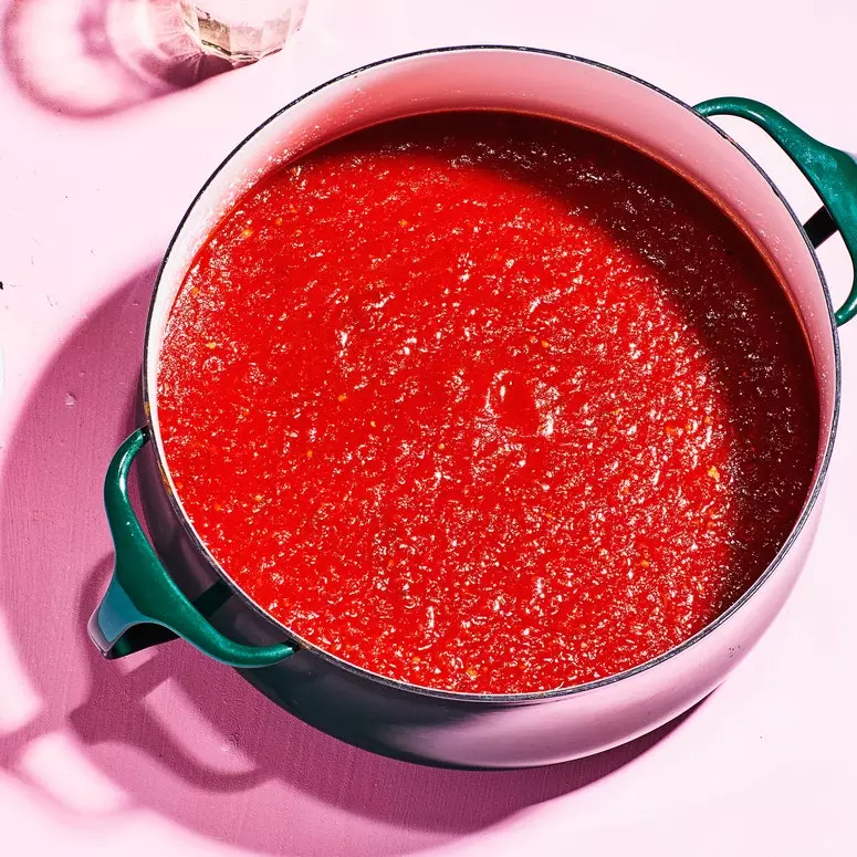 Isang teal twohandled pot na puno ng marinara sauce laban sa pink na background.