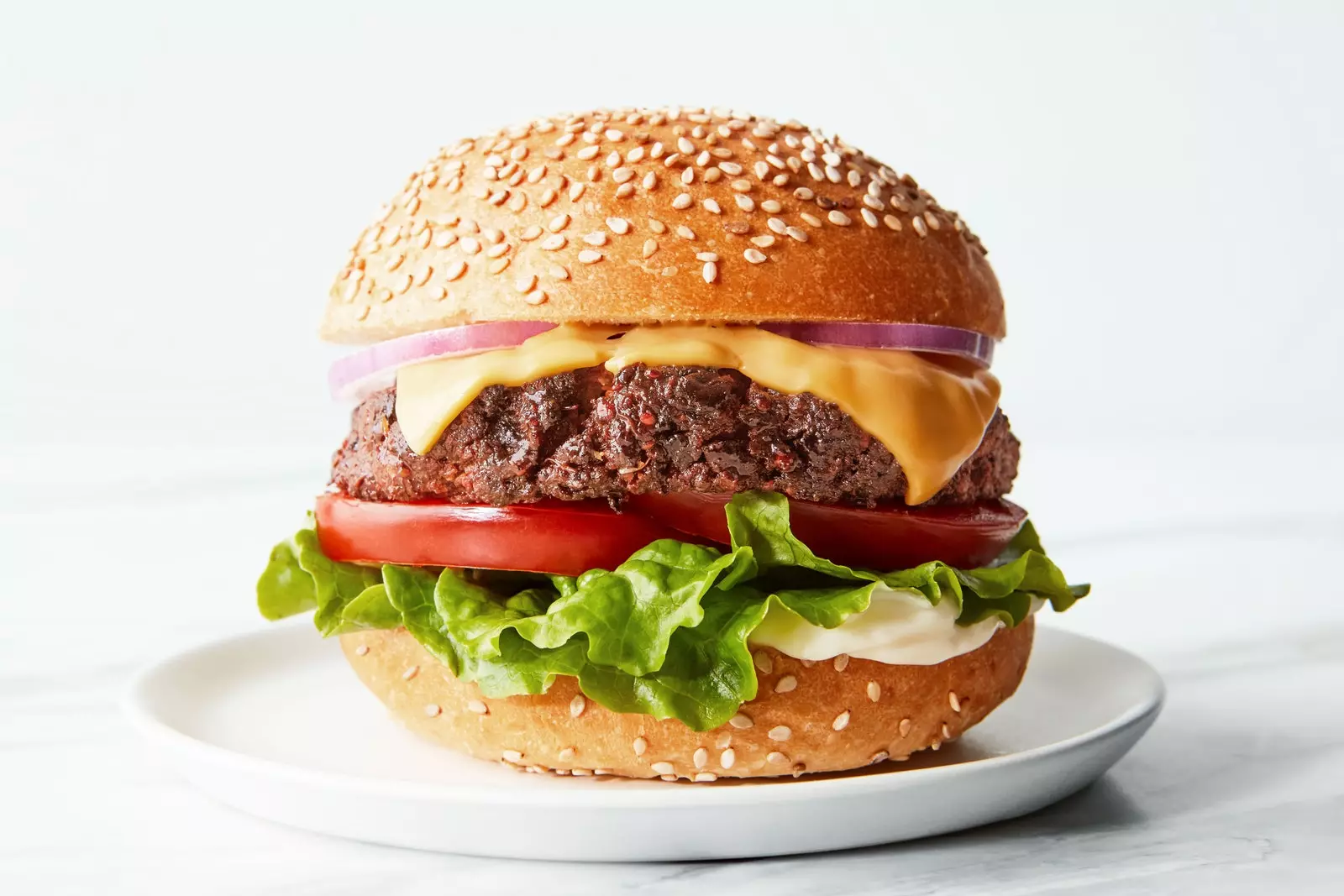 Foto de una hamburguesa de champiñones con queso, lechuga, tomate, cebolla y mayonesa en un panecillo.