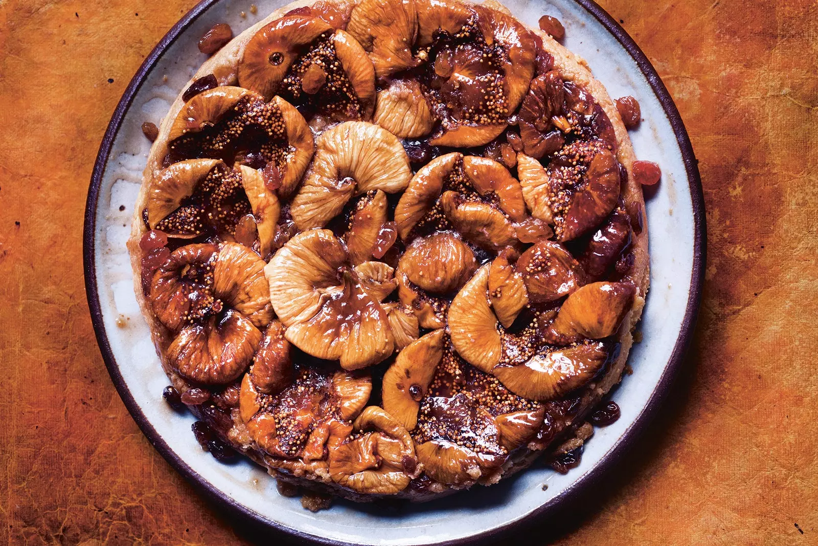 La crostata finita è stata capovolta su un piatto da portata, in mostra i fichi imbevuti di caramello compressi e l'uvetta dorata.