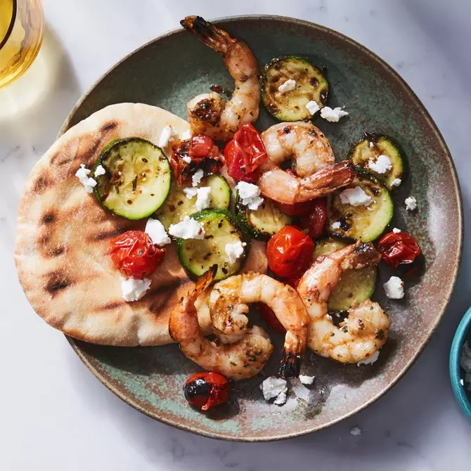 Foto van een van ons gunsteling garnale resepte Grieks-geïnspireerde geroosterde garnale met zucchini en tamaties op 'n bord met pita.