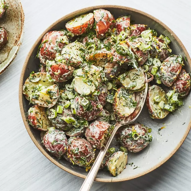 Litrato sa Creamy Potato Salad nga adunay Lemon ug Fresh Herbs sa usa ka mabaw nga panaksan nga adunay usa ka kutsara ug gamay nga kilid nga plato.