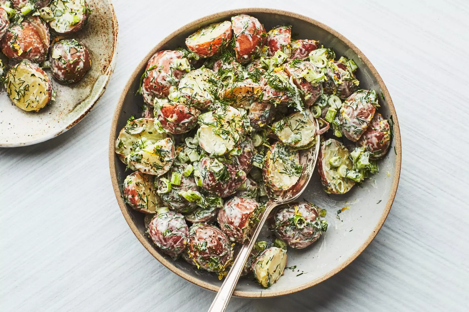 Litrato sa Creamy Potato Salad nga adunay Lemon ug Fresh Herbs sa usa ka mabaw nga panaksan nga adunay usa ka kutsara ug gamay nga kilid nga plato.