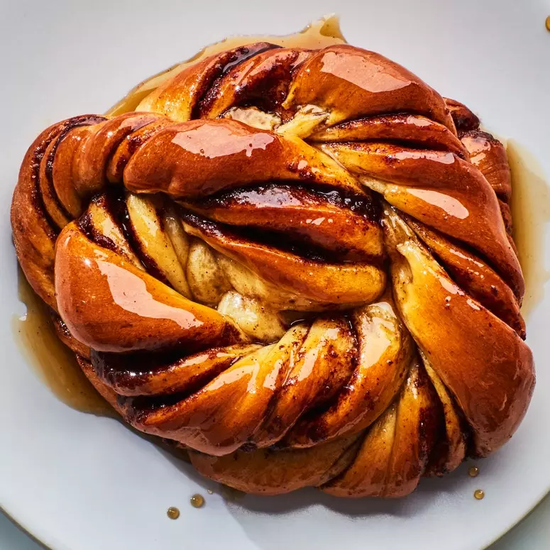 Un bollo de canela y cardamomo glaseado en un plato blanco.