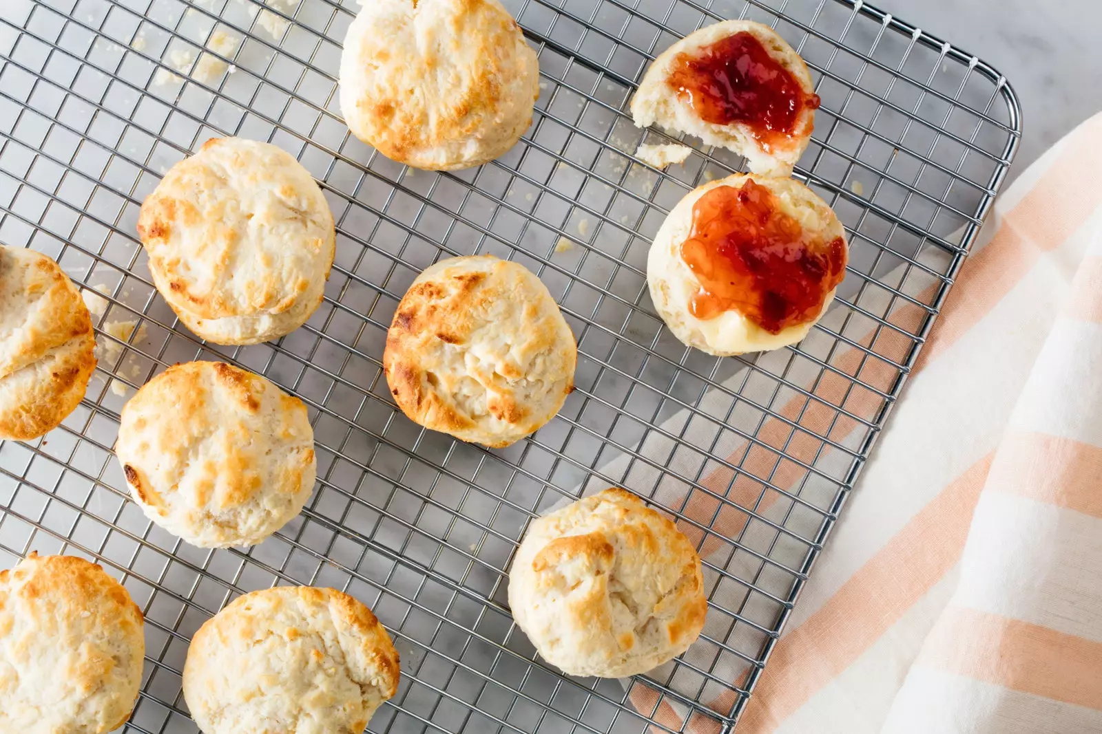 Plusieurs biscuits à trois ingrédients sur une grille de refroidissement avec l'un d'eux recouvert de confiture.