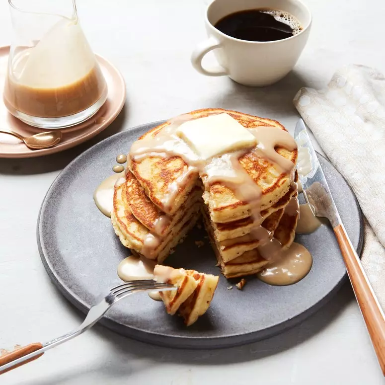 Gourmet's SourCream Pancakes พร้อม SourCream Maple Syrup บนจานที่มีมีดส้อมและกาแฟอยู่ด้านข้าง
