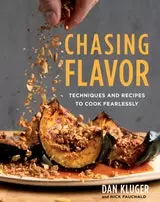 Kulinarijos knygos viršelis, kuriame pavaizduota šefo ranka, apibarstanti pikantiška granola ant skrudintų gilių moliūgų.