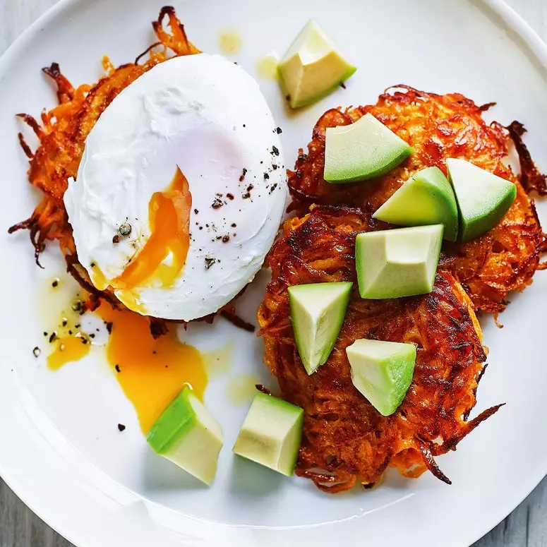 Wie man ein Ei pochiert Ein durchstochenes flüssiges Ei auf geriebenen Süßkartoffelpfannkuchen mit Avocadowürfeln.