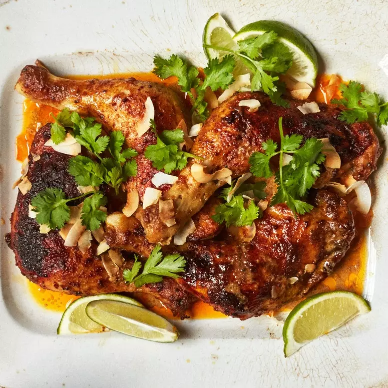 Patas de pollo bruñidas apiladas en un plato y adornadas con hojuelas de coco tostadas, rodajas de lima y cilantro.