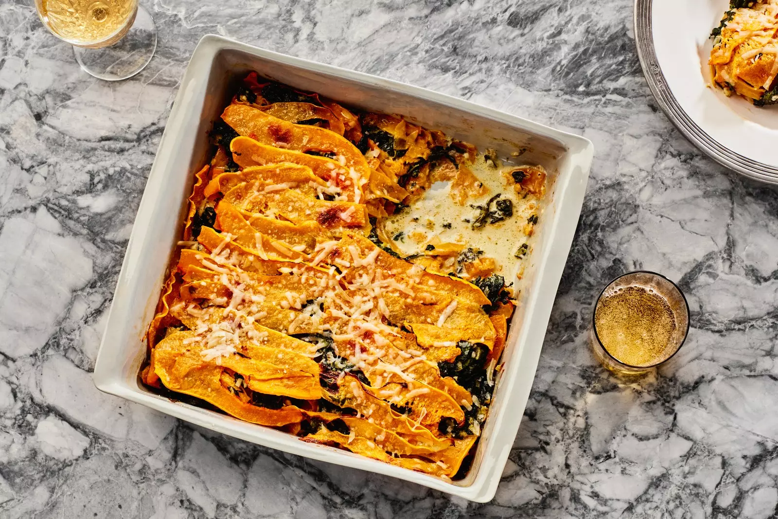 Butternut Squash ati Ipara Spinach Gratin ninu satelaiti pẹlu ounjẹ ti a mu jade ati gilasi waini kan ni ẹgbẹ