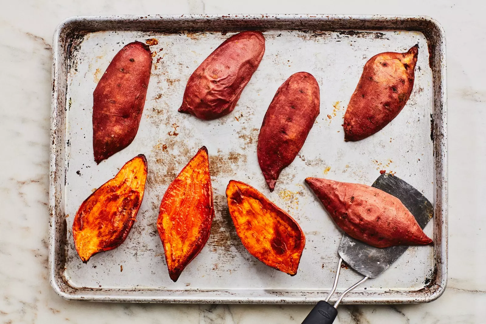 Batatas cortadas a la mitad asadas con la carne hacia abajo en una bandeja para hornear, algunas vueltas hacia arriba para revelar una superficie caramelizada.