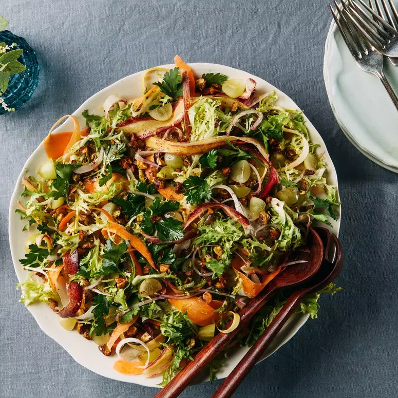 O salată de panglici frise și morcovi cu o vinaigretă de za'atarlemon pe o farfurie albă ustensile de servire din lemn și un teanc de...