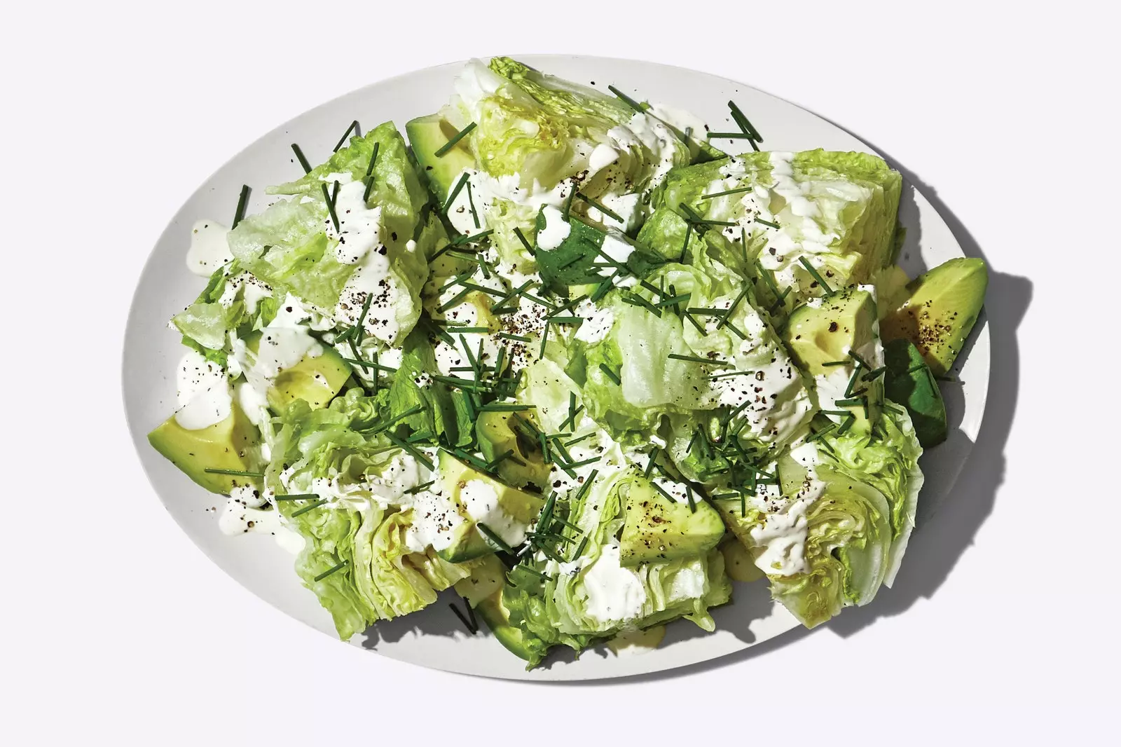 Malé kousky nakrájeného neodděleného ledového salátu přelité pažitkou a avokádem a krémovým dresinkem.