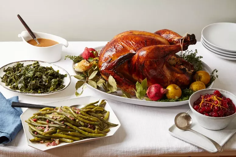 Foto af et bord dækket til Thanksgiving Dinner. En kalkun på et serveringsfad er omgivet af plader med grønne bønner, tranebær og sovs.