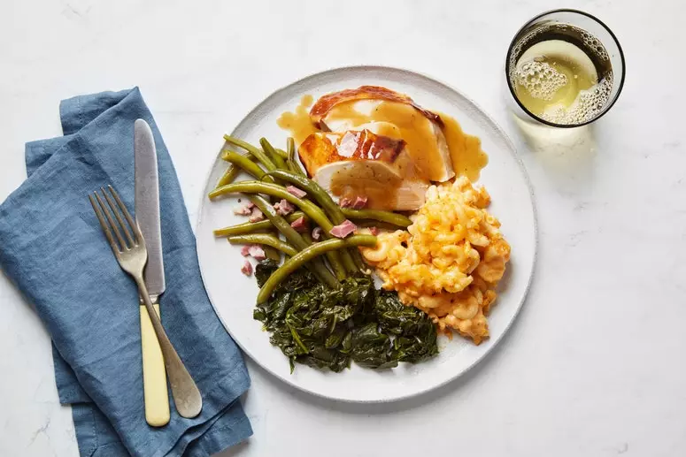 Une assiette de dîner de Thanksgiving avec de la dinde, des haricots, des légumes verts et du macaroni au fromage.