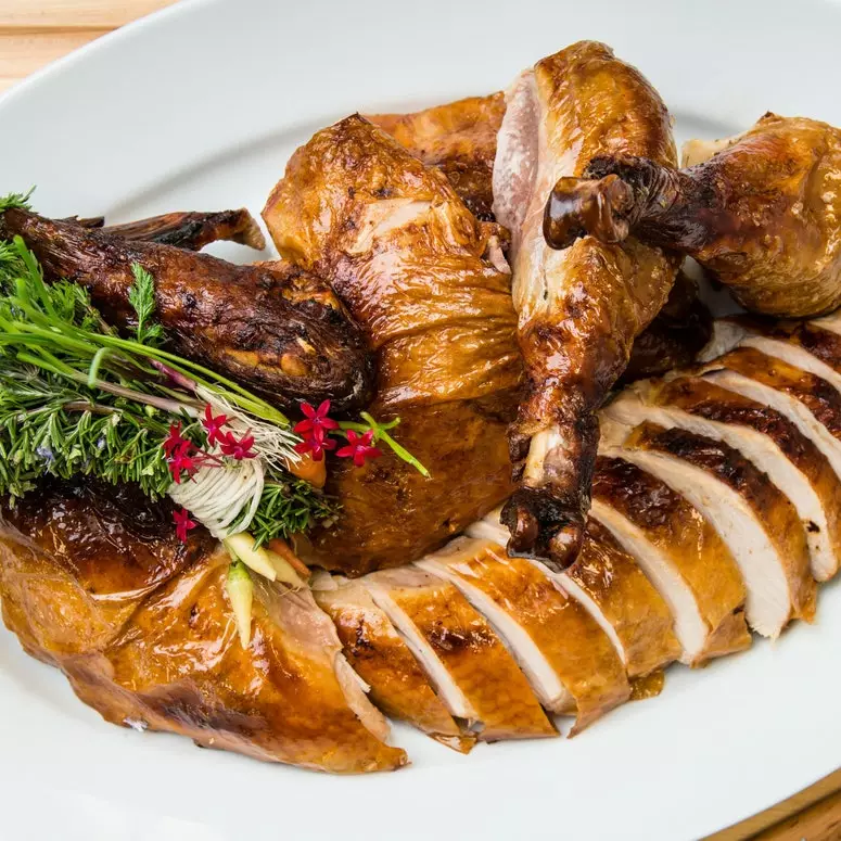 Rebanadas e patas de pavo asado de Thomas Keller da nosa mellor receita de pavo asado nun prato branco con guarnición verde.