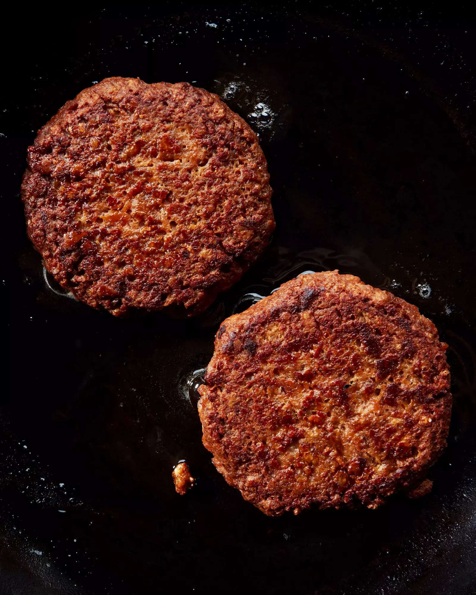 Foto de dos hamburguesas vegetarianas cocinándose en una sartén.