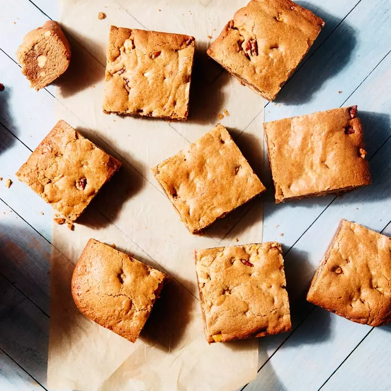 En batch af blondie firkanter på en marmor chevronstribet overflade ved siden af en kop mælkeagtig te.