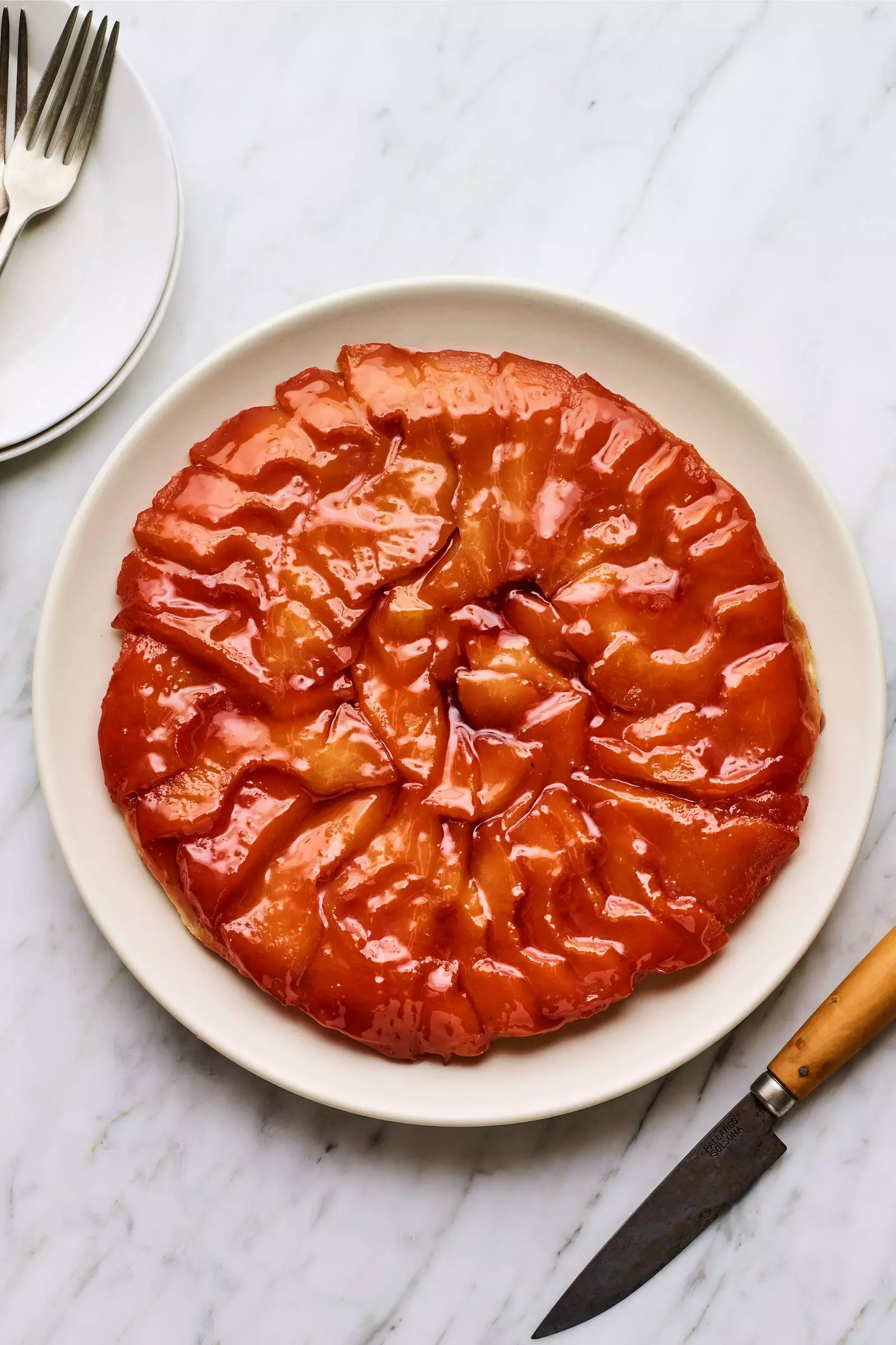 Foto di una torta di mele cotogne e mandorle su un piatto con coltello e forchette a lato.