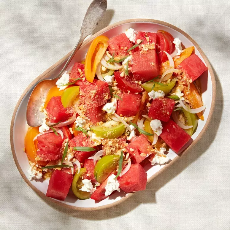 Insalata di pomodori all'anguria con formaggio di capra e noci di mais in un piatto da portata con un cucchiaio da portata.