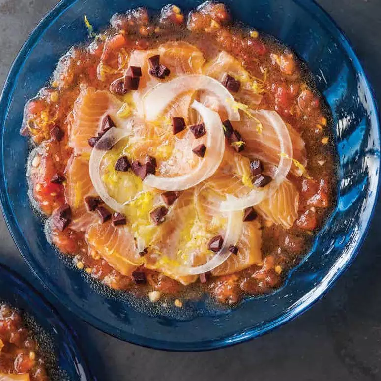 Truta curada com tomate azeitona preta e cebola em uma tigela azul.