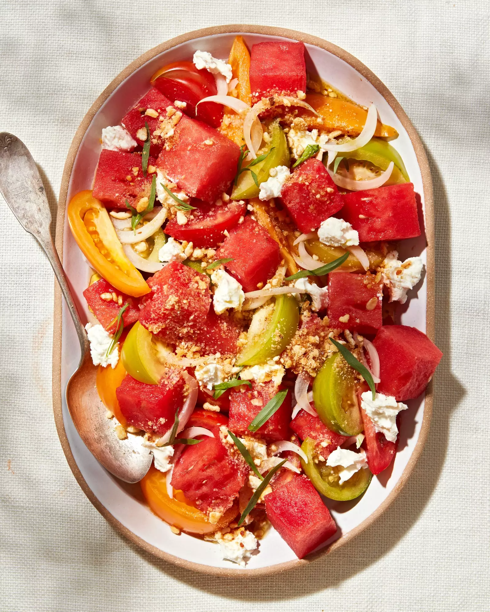 Insalata di pomodori all'anguria con formaggio di capra e noci di mais in un piatto da portata con un cucchiaio da portata.